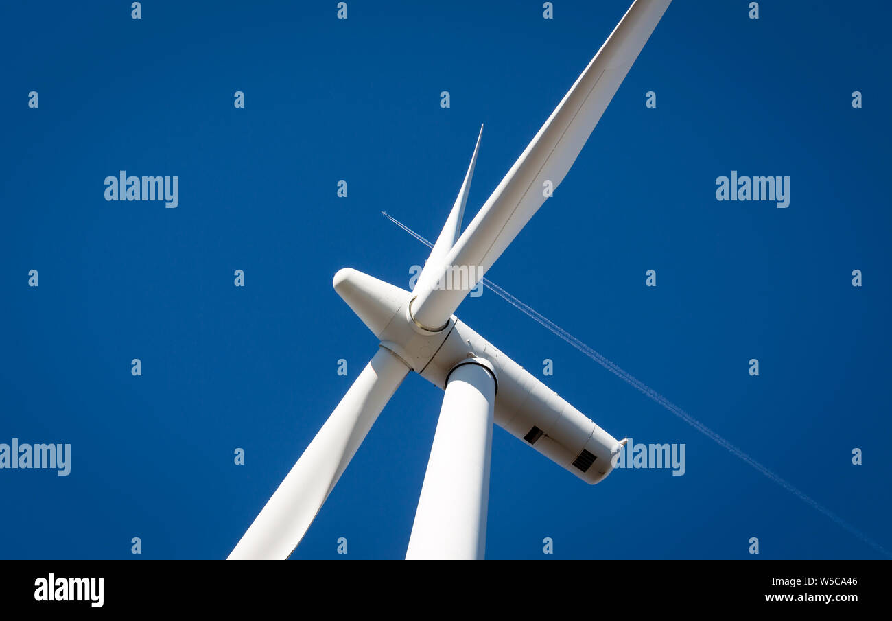 A wind turbine against a blue sky, with an airplane passing by in the ...