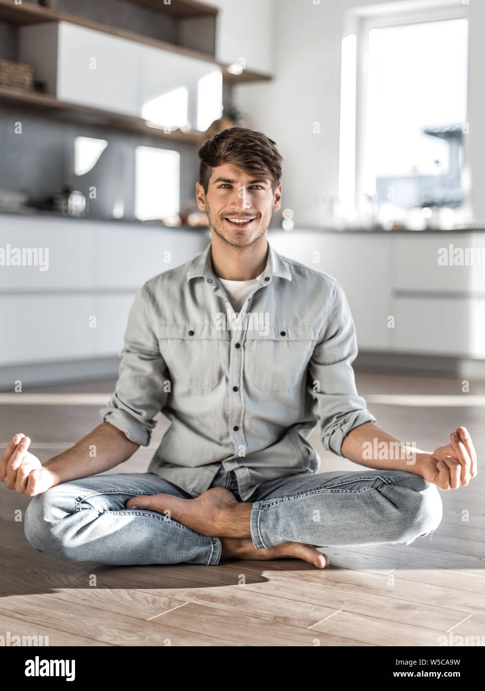 smiling young man sitting in Lotus position on kitchen floor Stock ...
