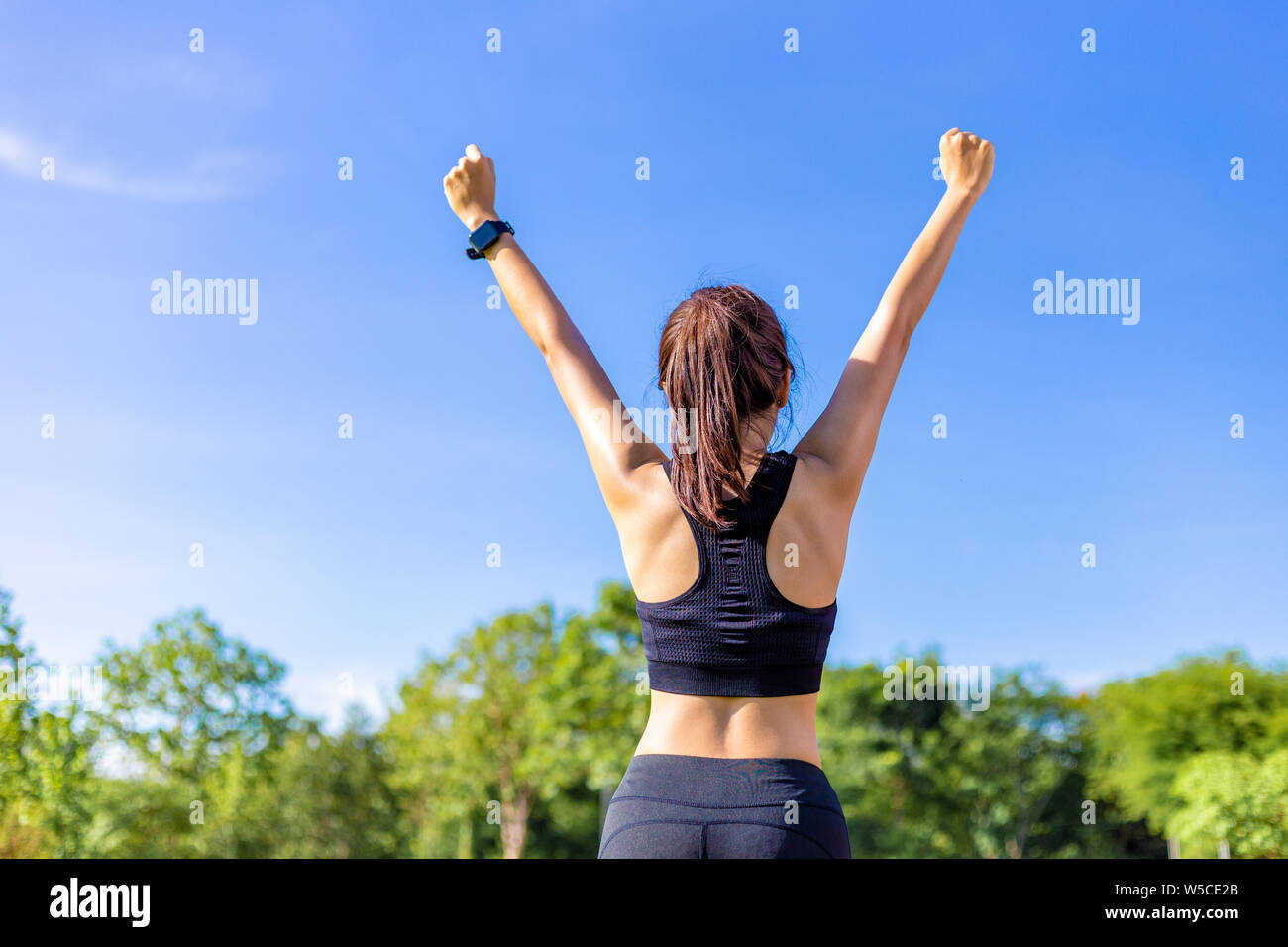 Happy young Asian woman raising up her arms cheerfully after complete ...