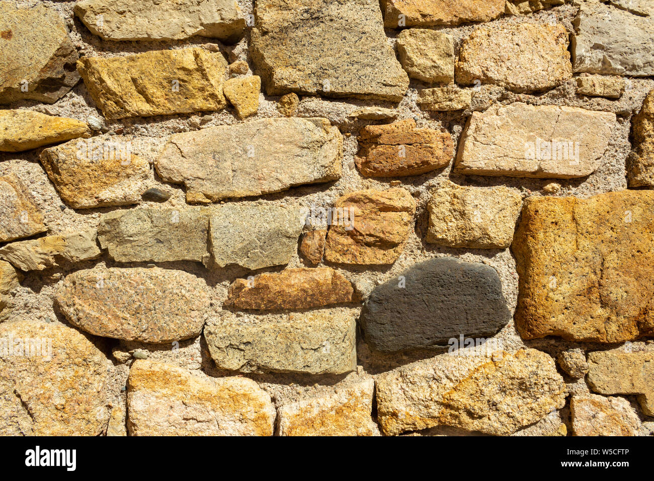 Detail of a stone wall made up of irregular shaped and coloured stone ...