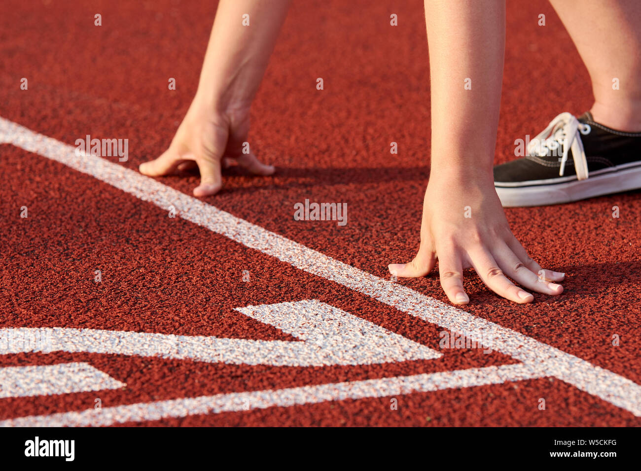 View of female athlete at race start. It stands on a red tartan track ...