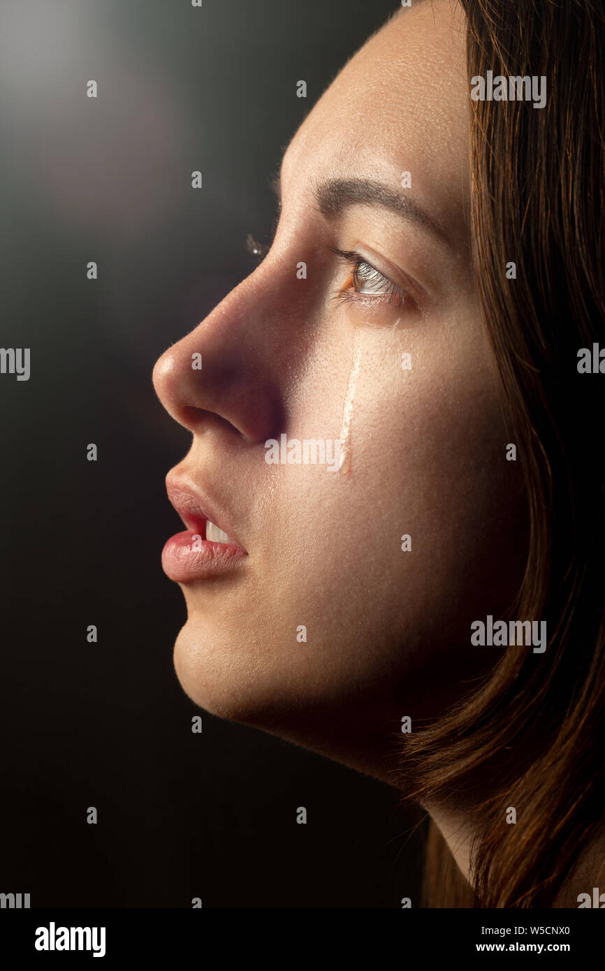 sad woman crying, looking aside on black background with light rays ...