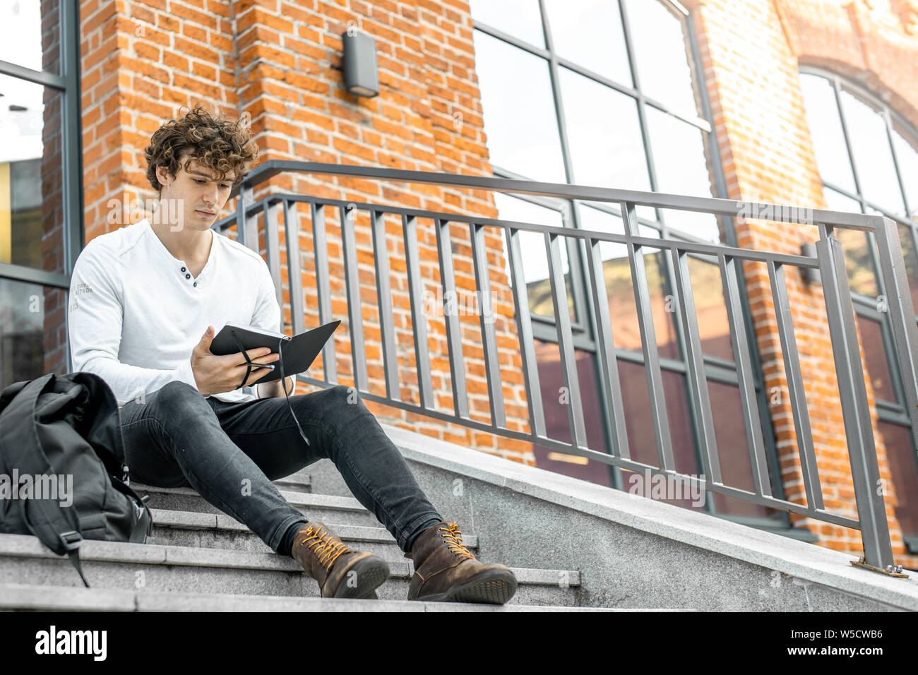 Attractive pensive man making notes in his black notepad and sitting on ...