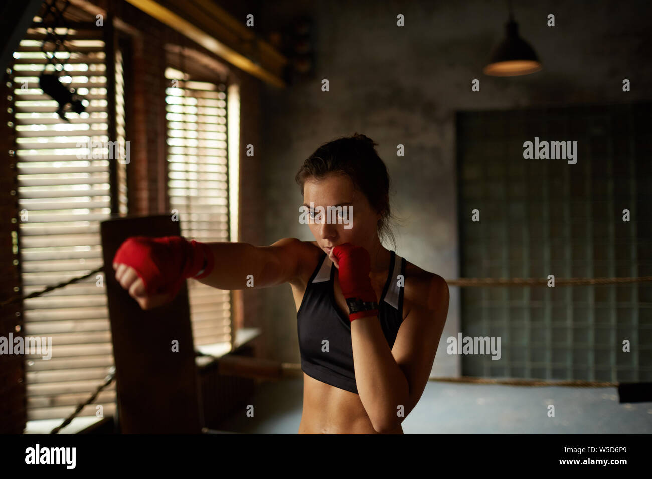 Dramatic portrait of tough female boxer practicing in boxing ring, copy ...