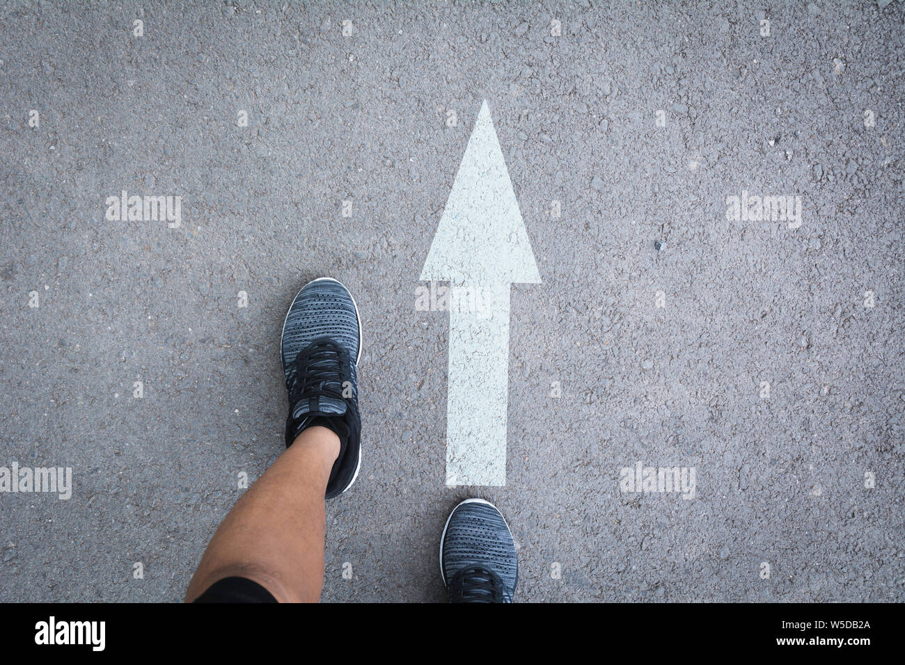 Top view of man wearing shoes choosing a way marked with white arrows ...