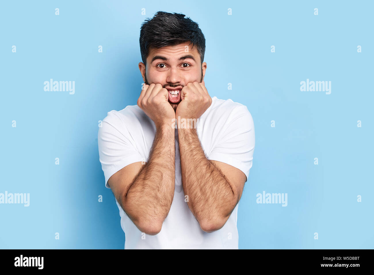 puzzled fearful handsome bearded man keeping fists near his chin ...