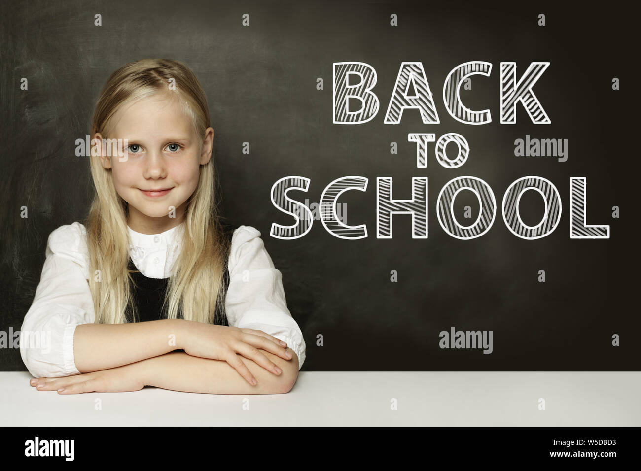 Smiling blonde child girl thinking on chalkboard. Back to school ...
