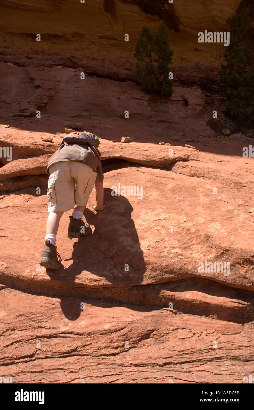 Young boy climbing up the red slickrock in the Davis Canyon ...