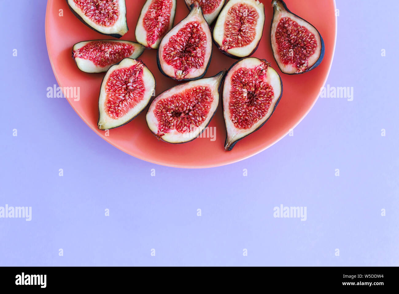 Ripe cutted figs on coral plate on violet background. Copy space. Top ...