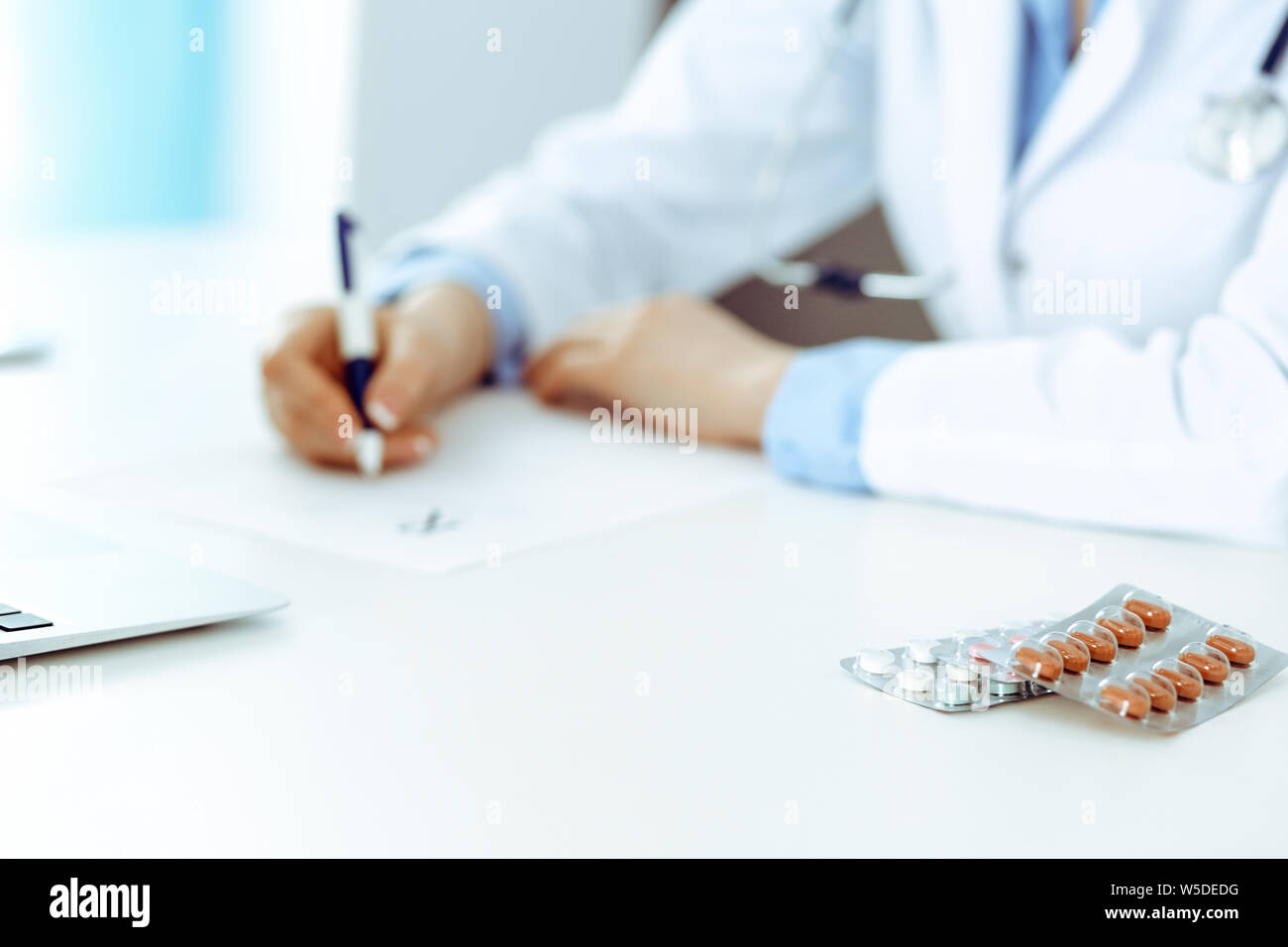 Female doctor filling up prescription form while sitting at the desk in ...