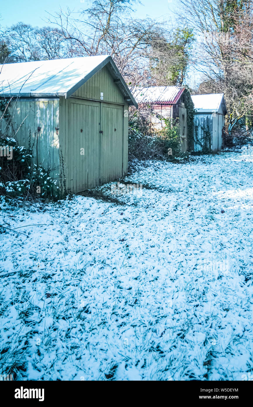 Three old wooden snow covered garages, with trees in the background ...