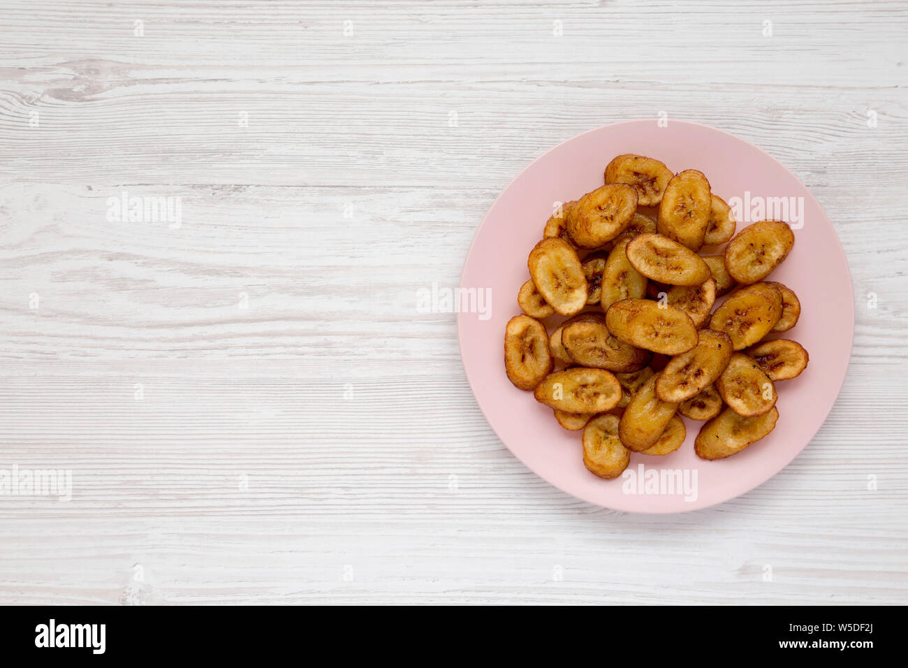 Top view, homemade fried plantains on a pink plate on a white wooden ...