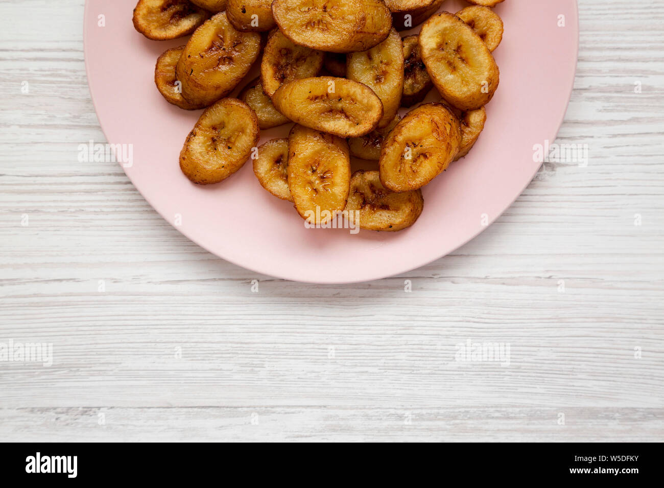Homemade fried plantains on a pink plate on a white wooden background ...