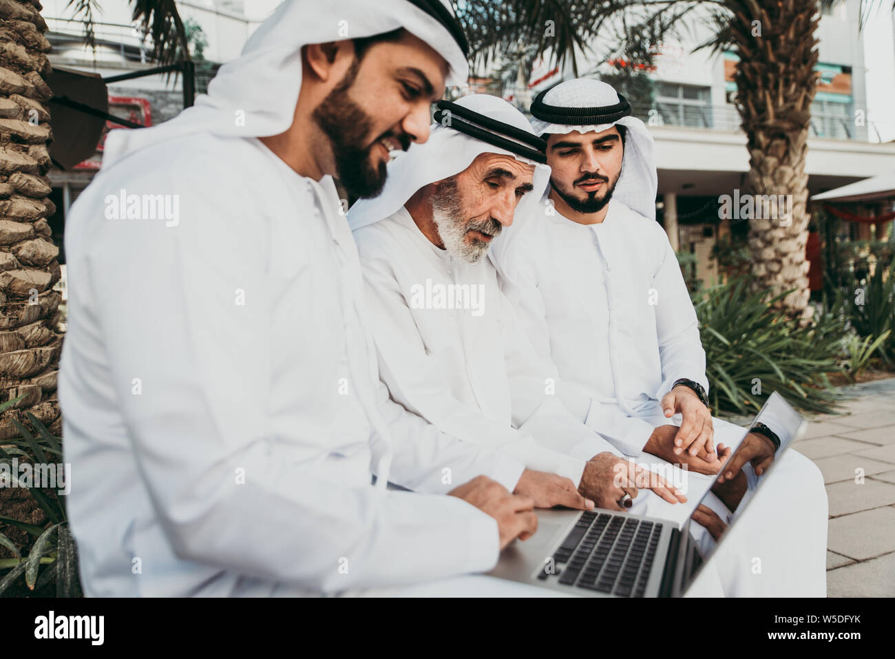 Three business men walking in Dubai wearing traditional emirati clothes ...