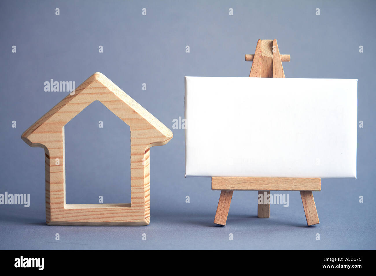 A wooden figure of house and white board on miniature easel on gray ...