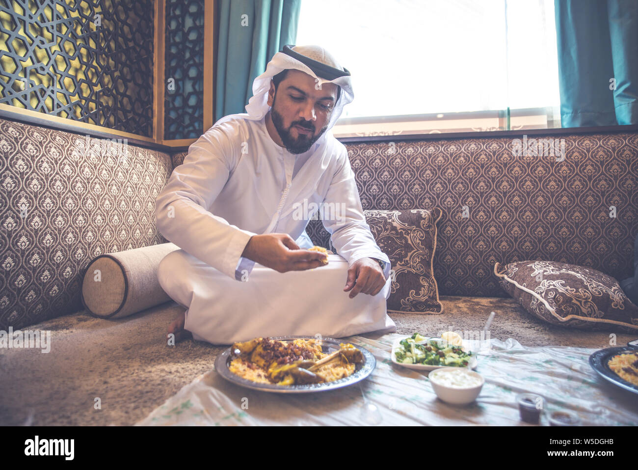 Arabic man with traditional clothes eating chicken mandy, in Dubai ...