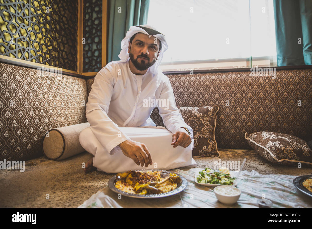 Arabic man with traditional clothes eating chicken mandy, in Dubai ...