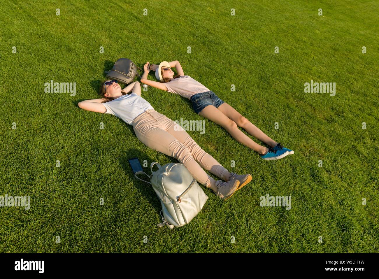 Two young female students with backpacks lying on green lawn grass. Top ...