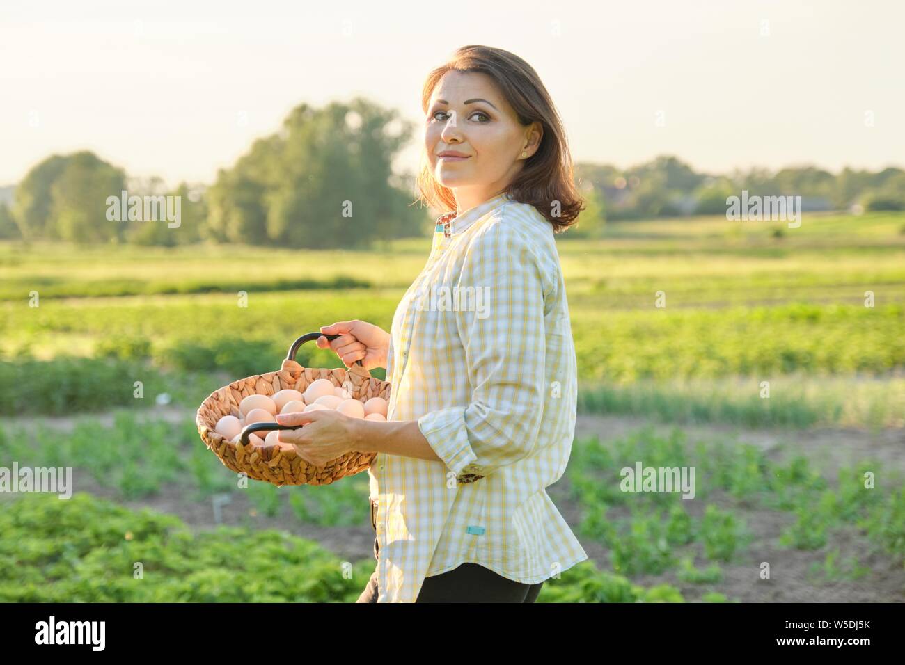 Outdoor portrait of farmer woman with basket of fresh chicken eggs ...