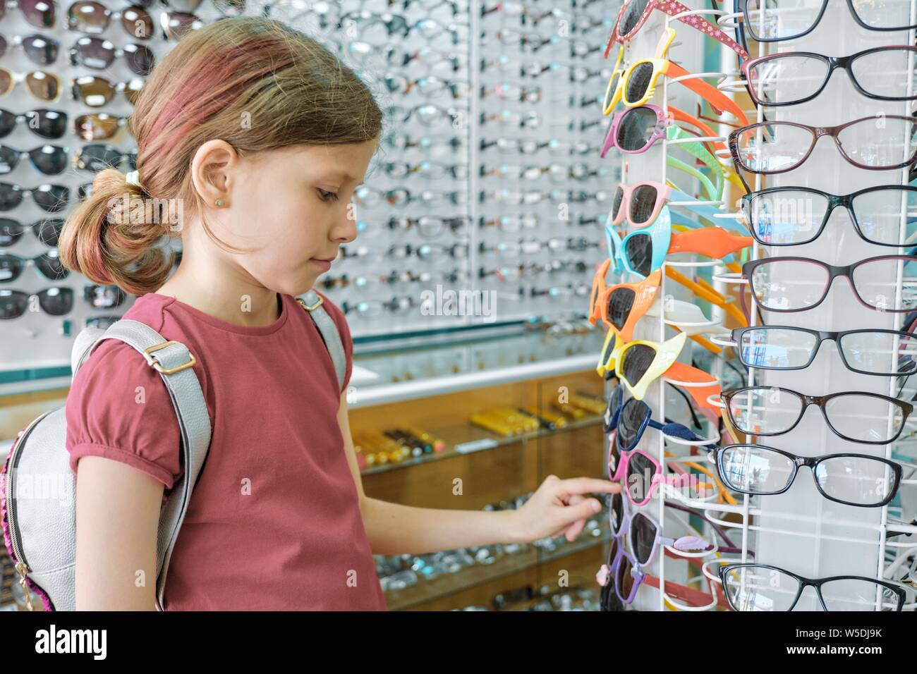 Girl looking and choosing sunglasses, child near shop window in eyewear ...