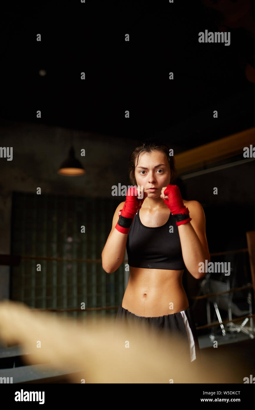 Dramatic front view portrait of tough female boxer practicing in boxing ...