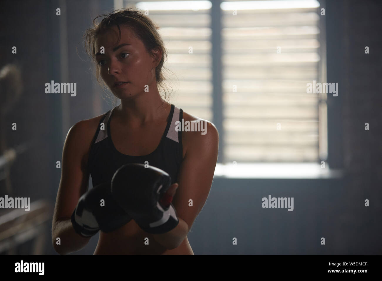 Dark toned portrait of sweaty young woman practicing boxing in sports ...