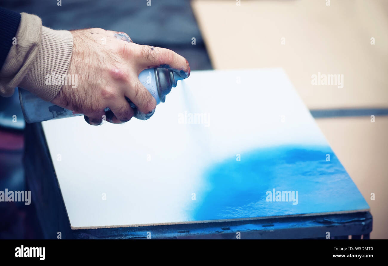 Hand daring artist holding a bottle of aerosol blue paint and pressing ...