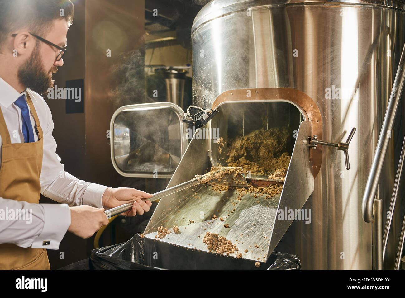 Handsome, adult brewery worker in glasses, white shirt and brown apron ...