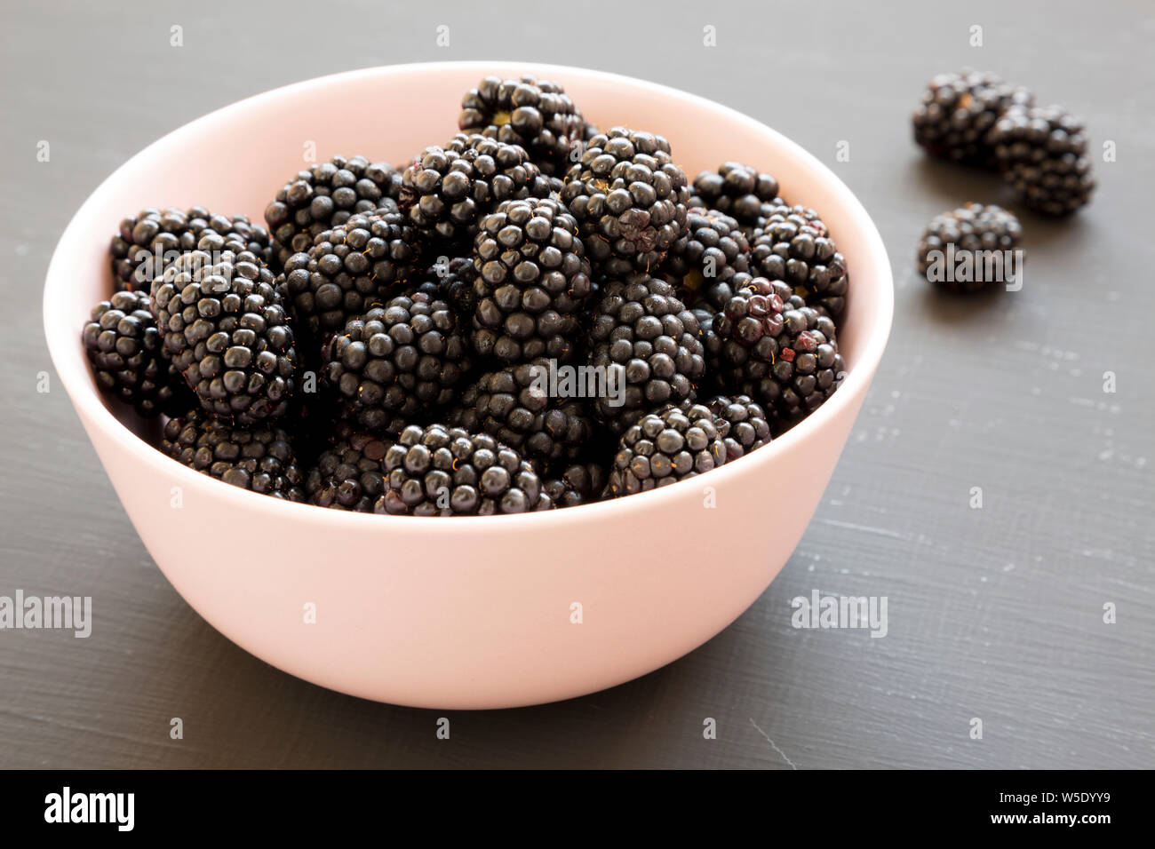 Blackberries in a pink bowl on a black background, side view. Summer ...