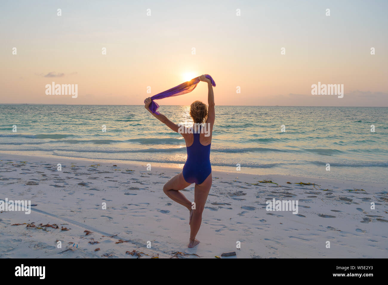 Woman performing yoga exercise on sand beach romantic sky at sunset ...