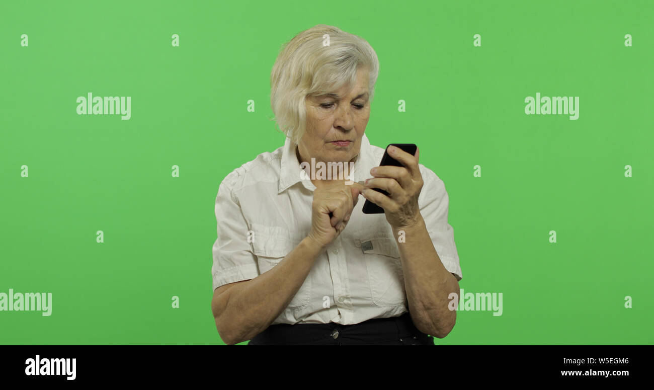 An elderly woman works on a smartphone. Old pretty grandmother in a ...