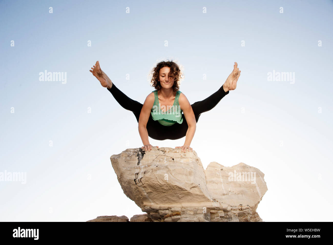 Yoga woman on a big rock balancing in the pose Firely or Titibasana ...
