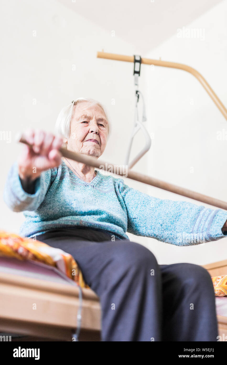 Elderly 96 years old woman exercising with a stick sitting on her bad ...