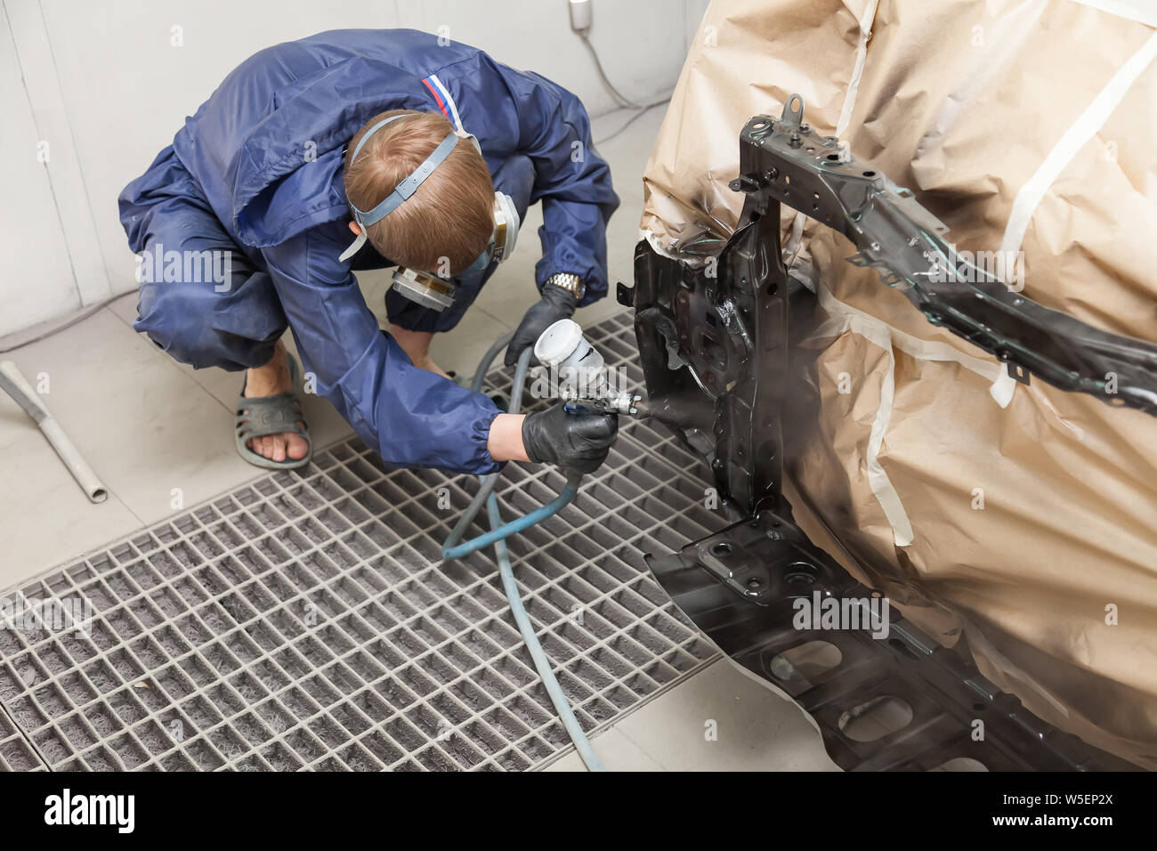 A male worker in jumpsuit and gloves paints with a spray gun a front ...
