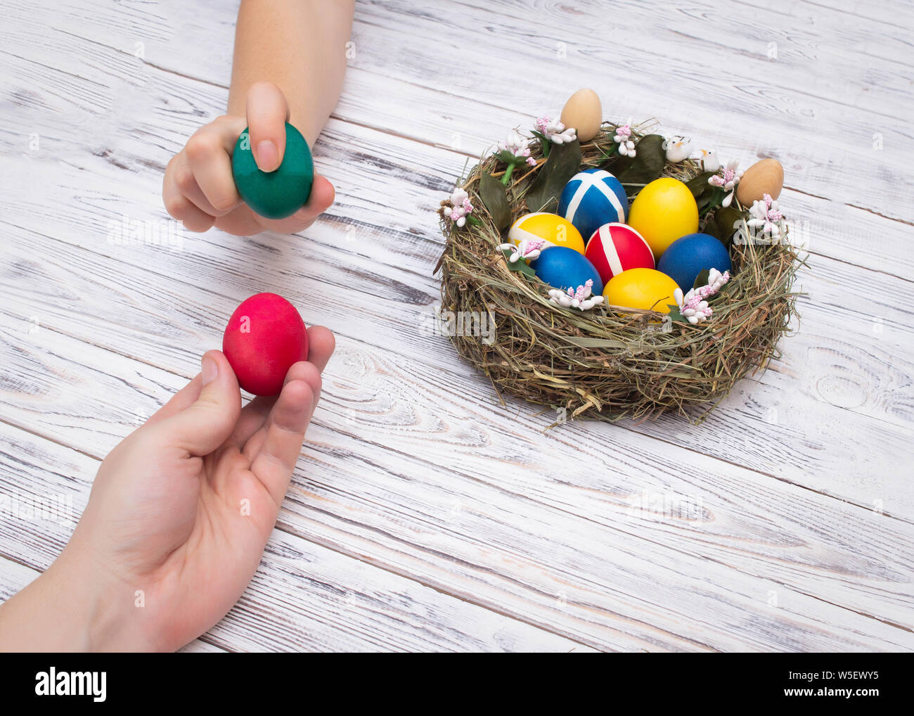 two people holding colorful chicken easter eggs on a white wooden ...