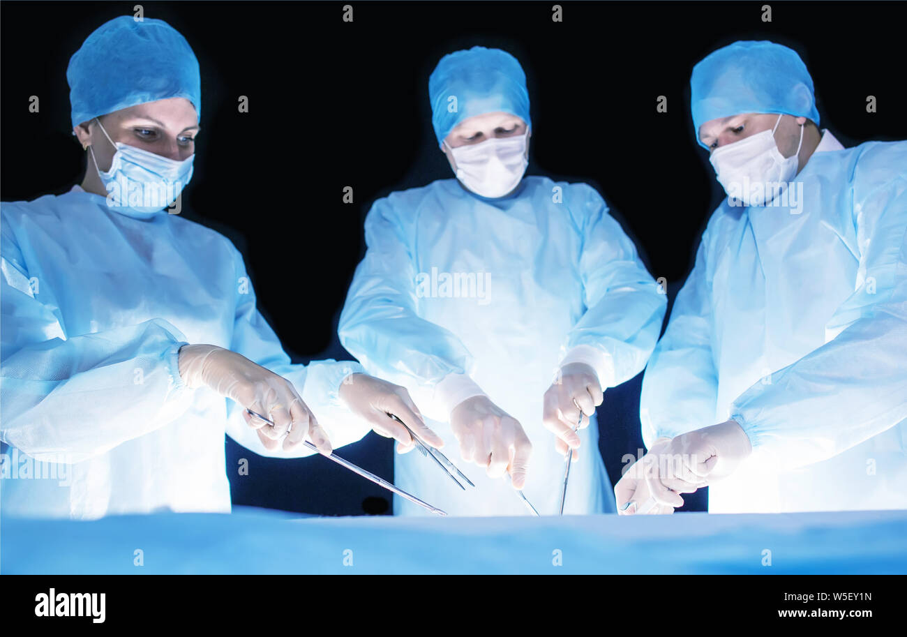 Three surgeons, a man and a woman, perform surgery in the operating ...