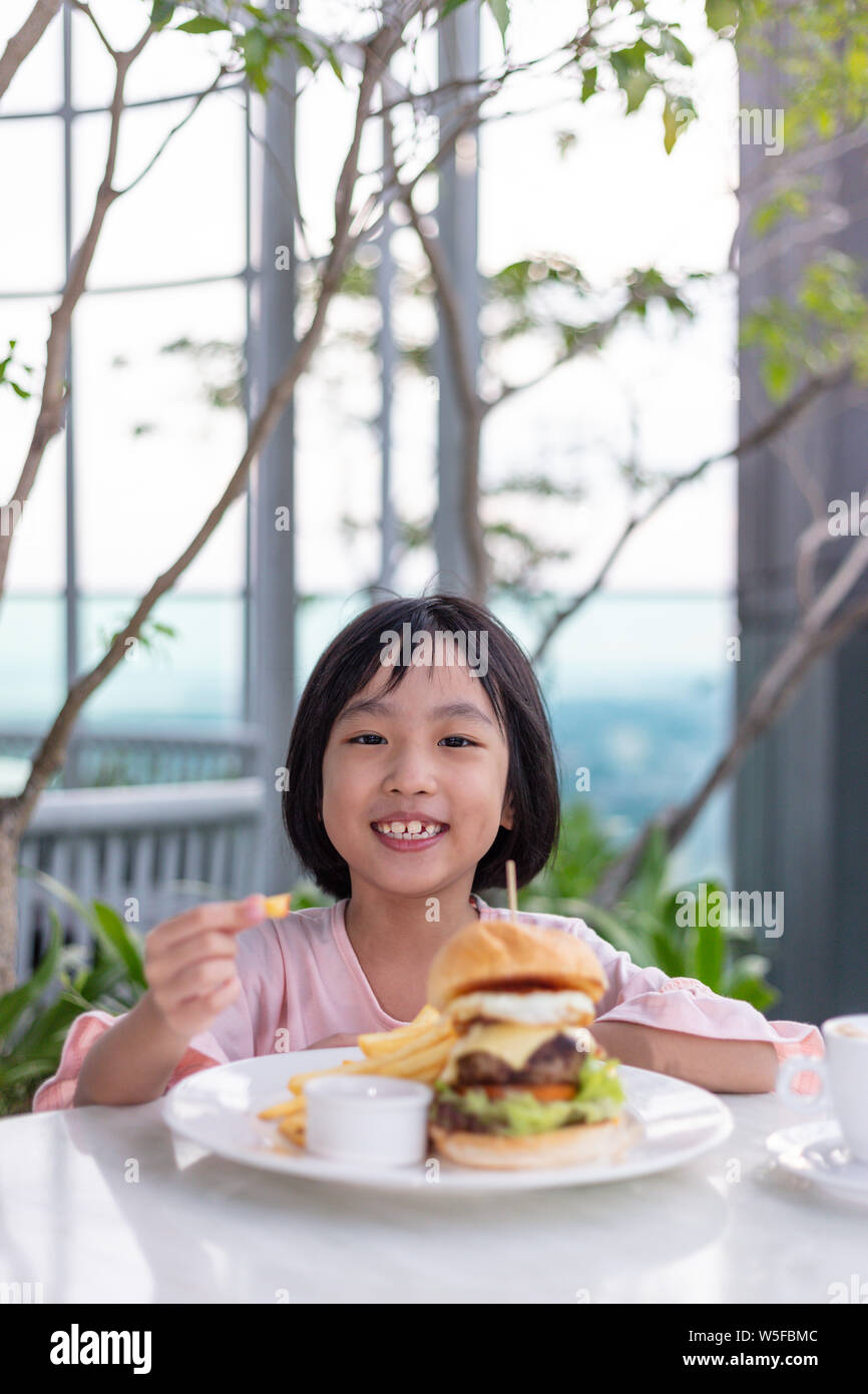 Asian Little Chinese Girl eating hamburger in the outdoor cafe Stock ...