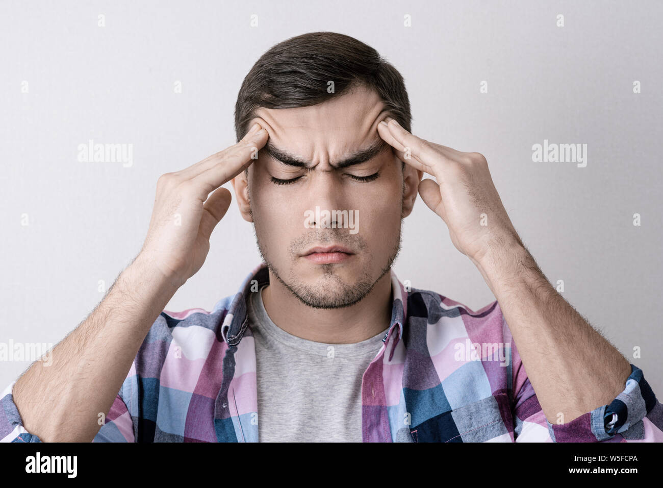 Portrait headshot of young caucasian man with headache, pressing his ...