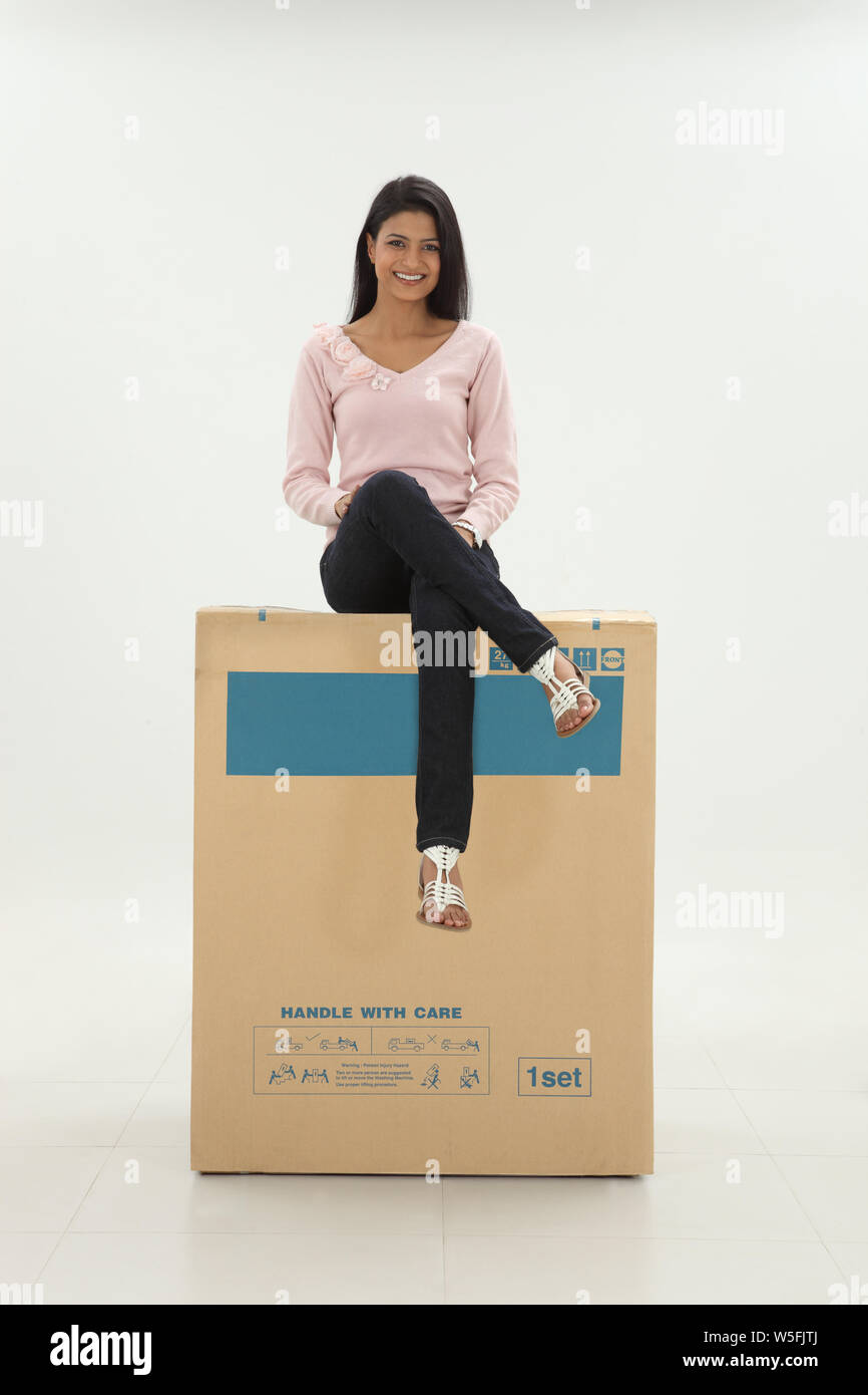 Woman sitting on a cardboard box and smiling Stock Photo - Alamy