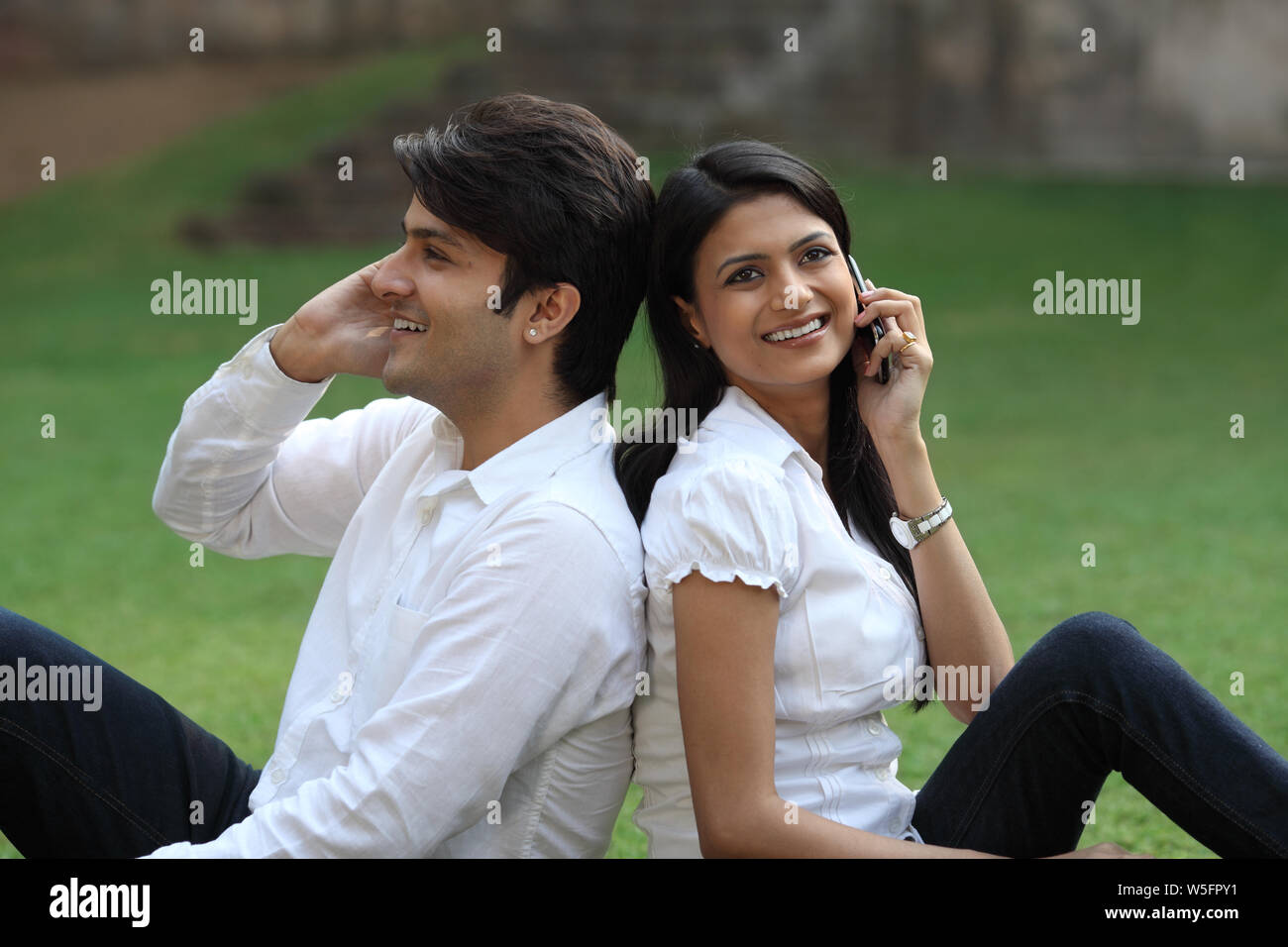 Couple sitting back to back and talking on mobile phones Stock Photo ...