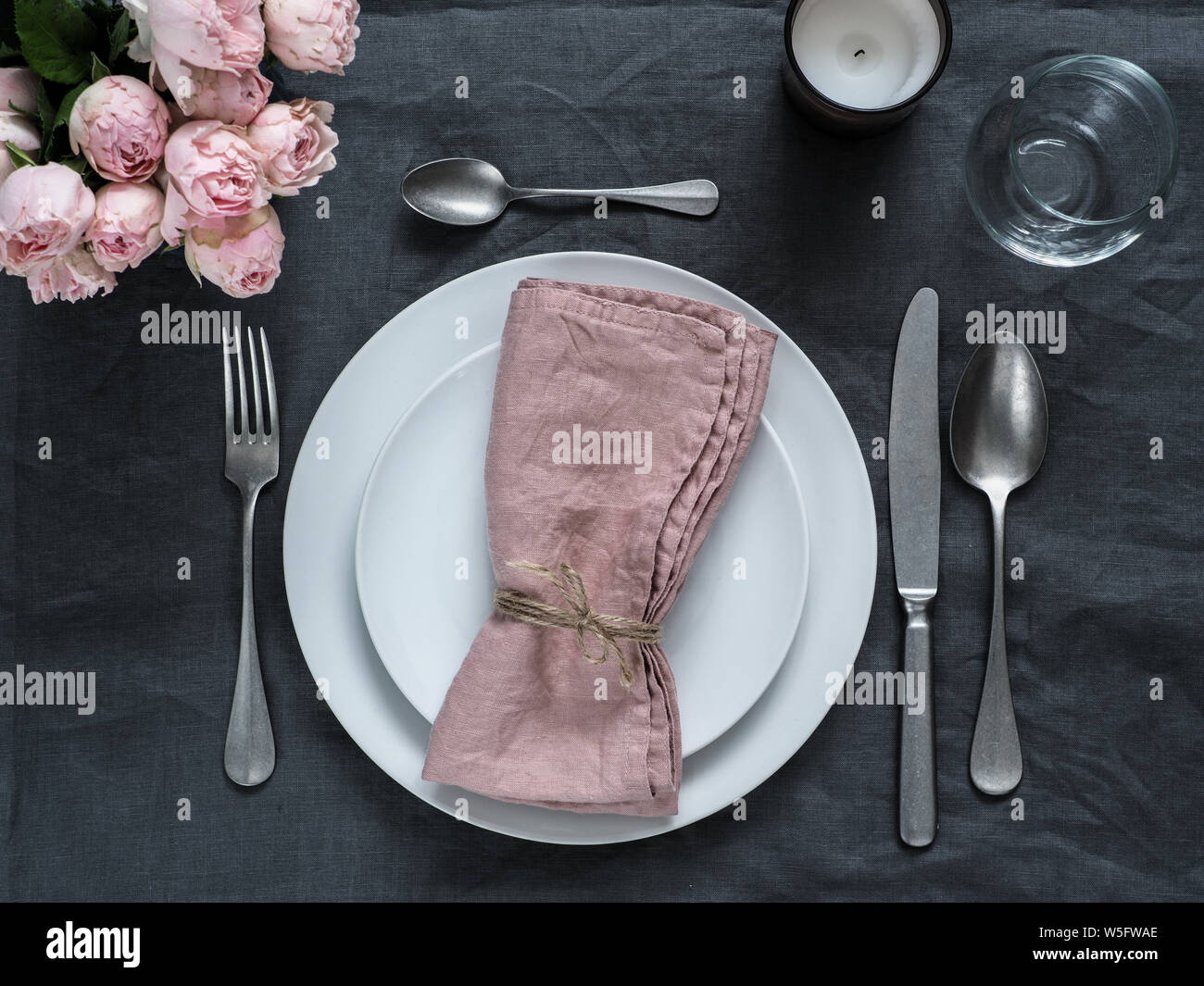 Beautiful table setting with pink spray roses and candle on gray linen ...