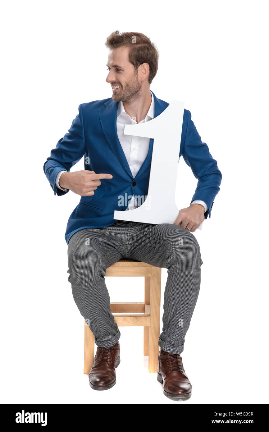 Young casual man pointing to a number one that he is holding on his lap ...