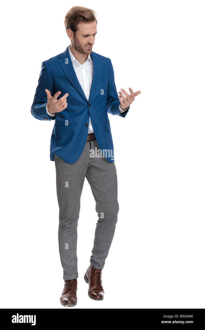 Thoughtful casual man stepping forward and looking at his hands while ...
