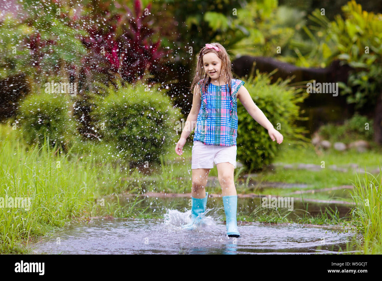 Kid playing out in the rain. Children with umbrella and rain boots play ...