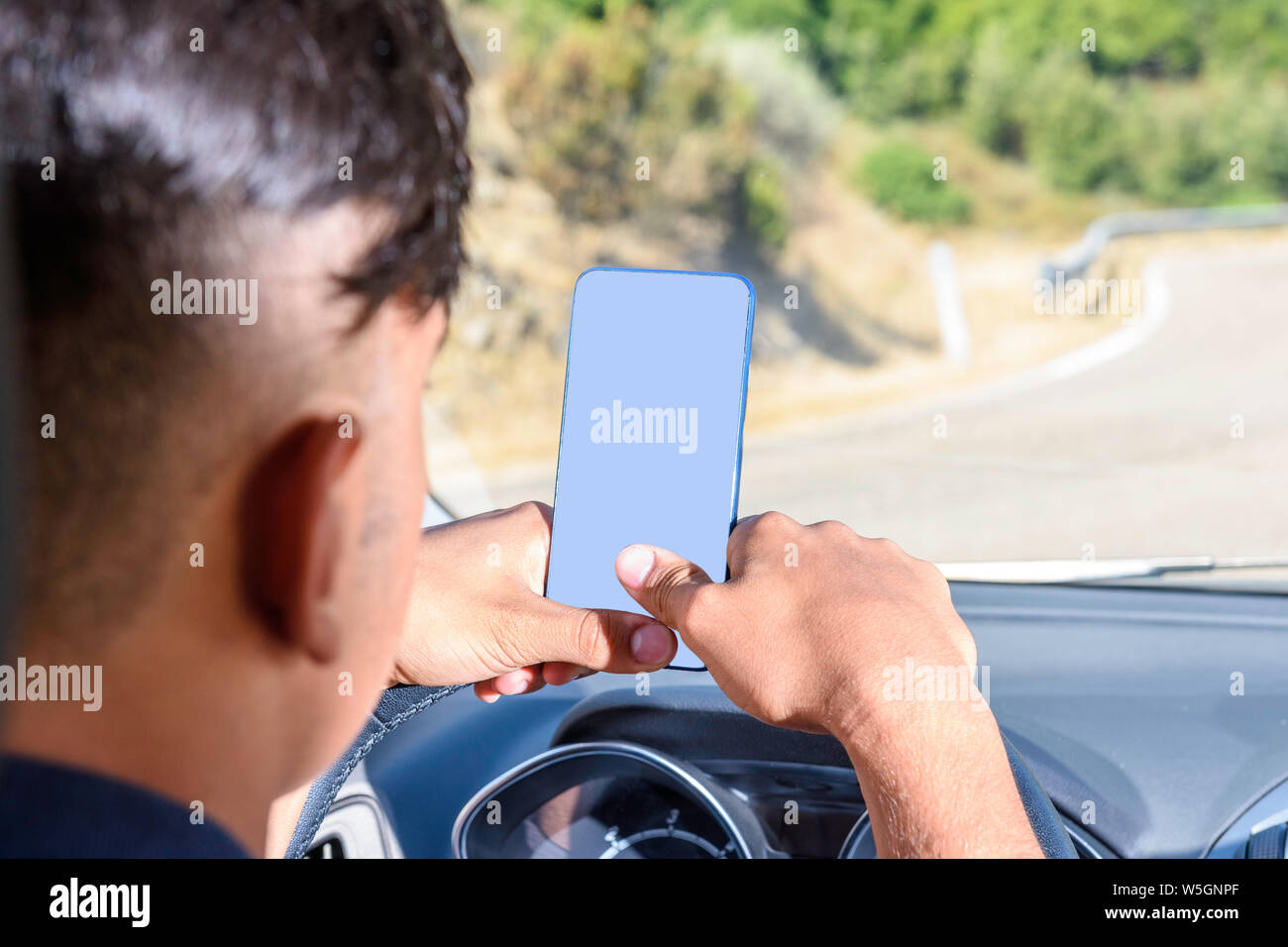Young driver, using smartphone, on the road in the car. Distraction and ...