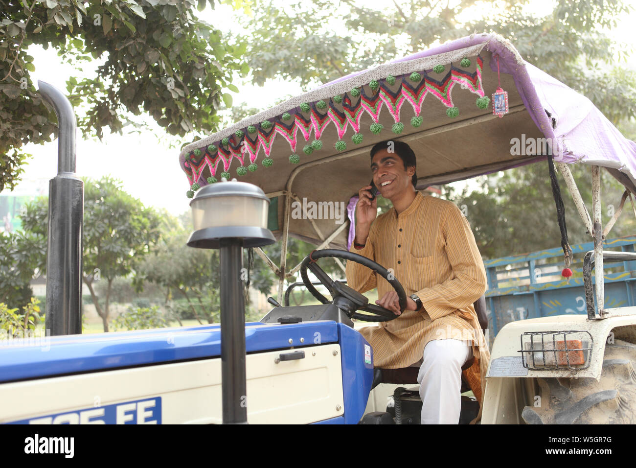 Farmer driving a tractor while talking on mobile phone Stock Photo - Alamy
