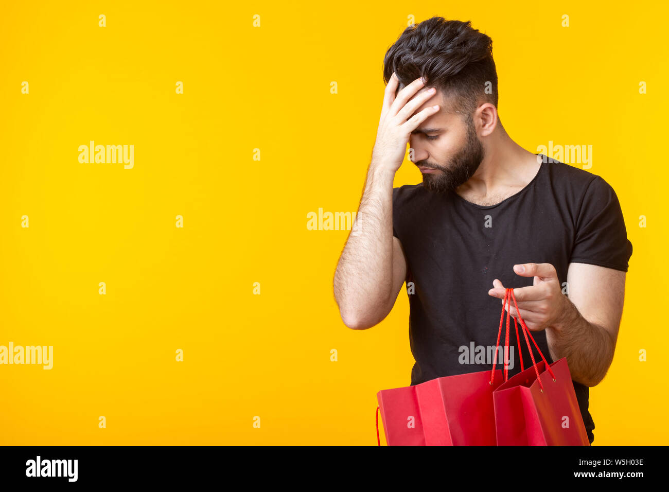 Cute young sad bearded man looks at the purchase in shopping bags on a ...