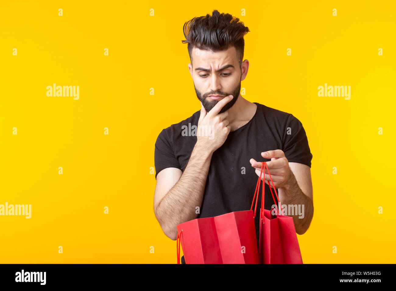 Cute young sad bearded man looks at the purchase in shopping bags on a ...