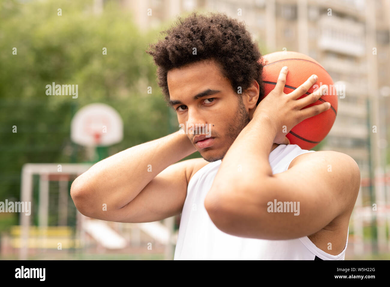 Young serious sportsman holding ball for playing basketball behind neck ...