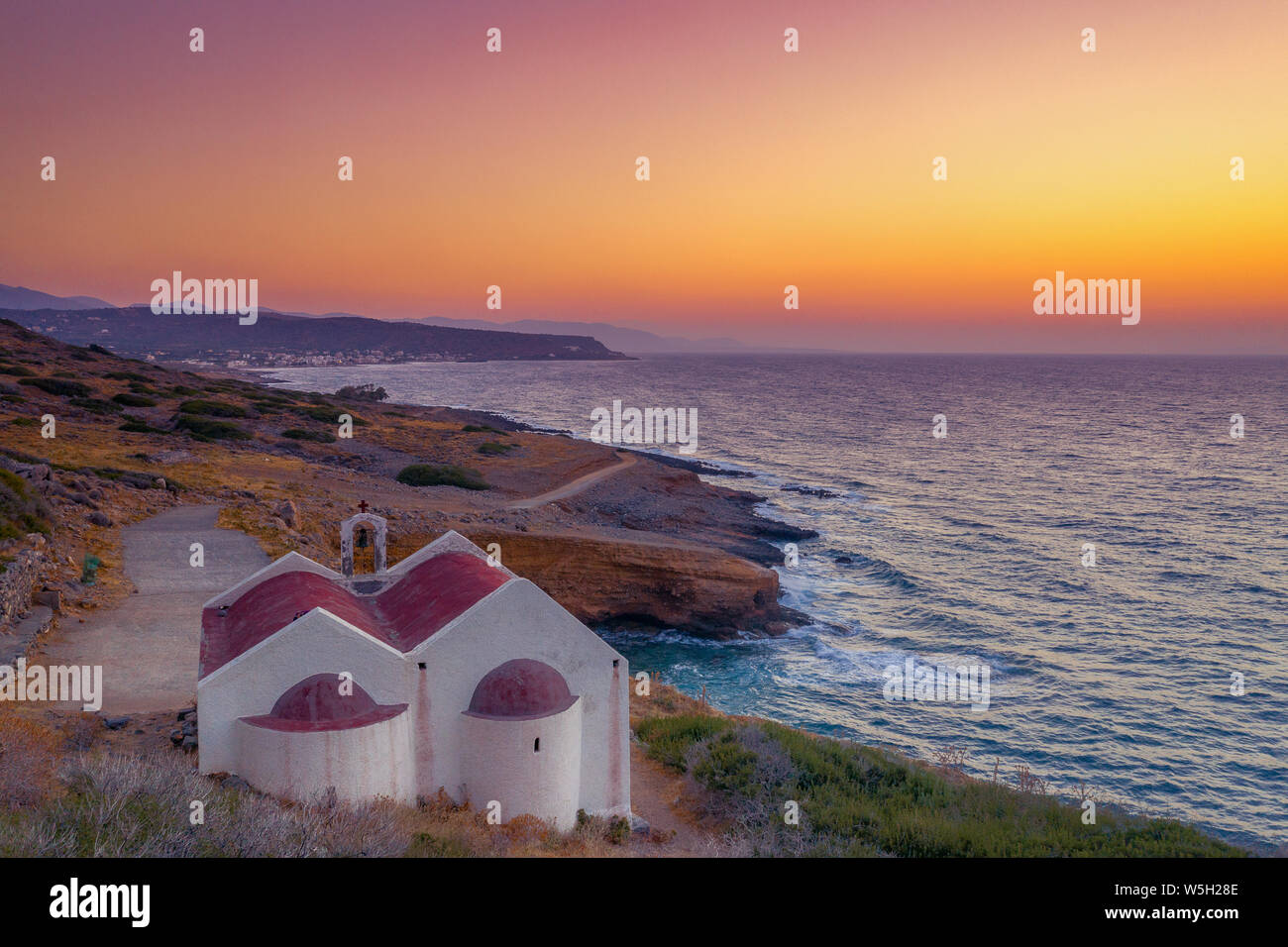 Gorgeus sunset over sea with waves, rocks and traditional greek village ...